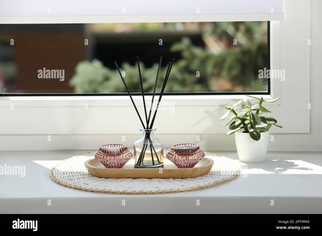 Reed diffuser with burning candles and houseplant on white window sill ...