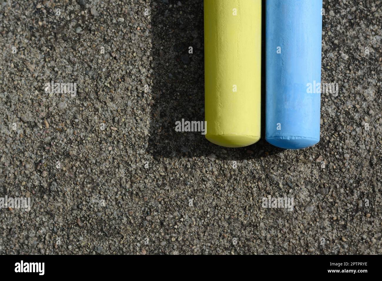 Yellow and light blue chalk sticks on asphalt, flat lay. Space for text ...