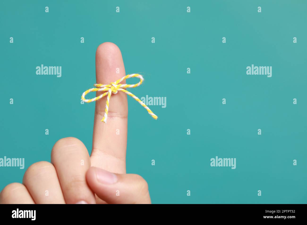 Man showing index finger with tied bow as reminder on turquoise ...