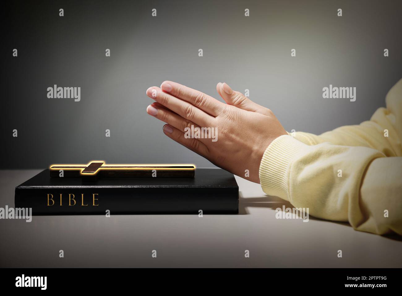 Woman praying over Bible with cross at white table against grey ...