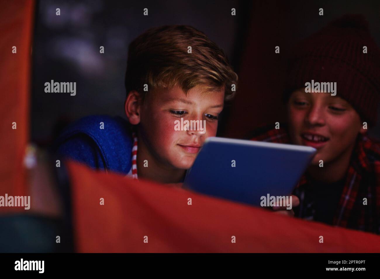 Warm and cozy in their tent with their tech. two young boys sharing a ...