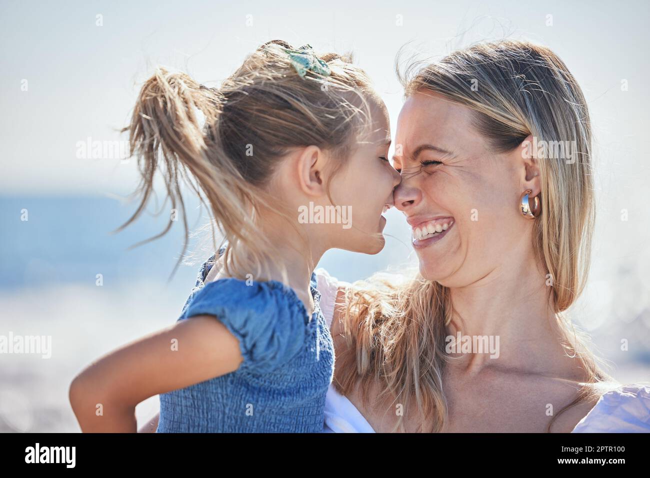 Adorable little daughter and mother rubbing noses while spending time together at the beach ...
