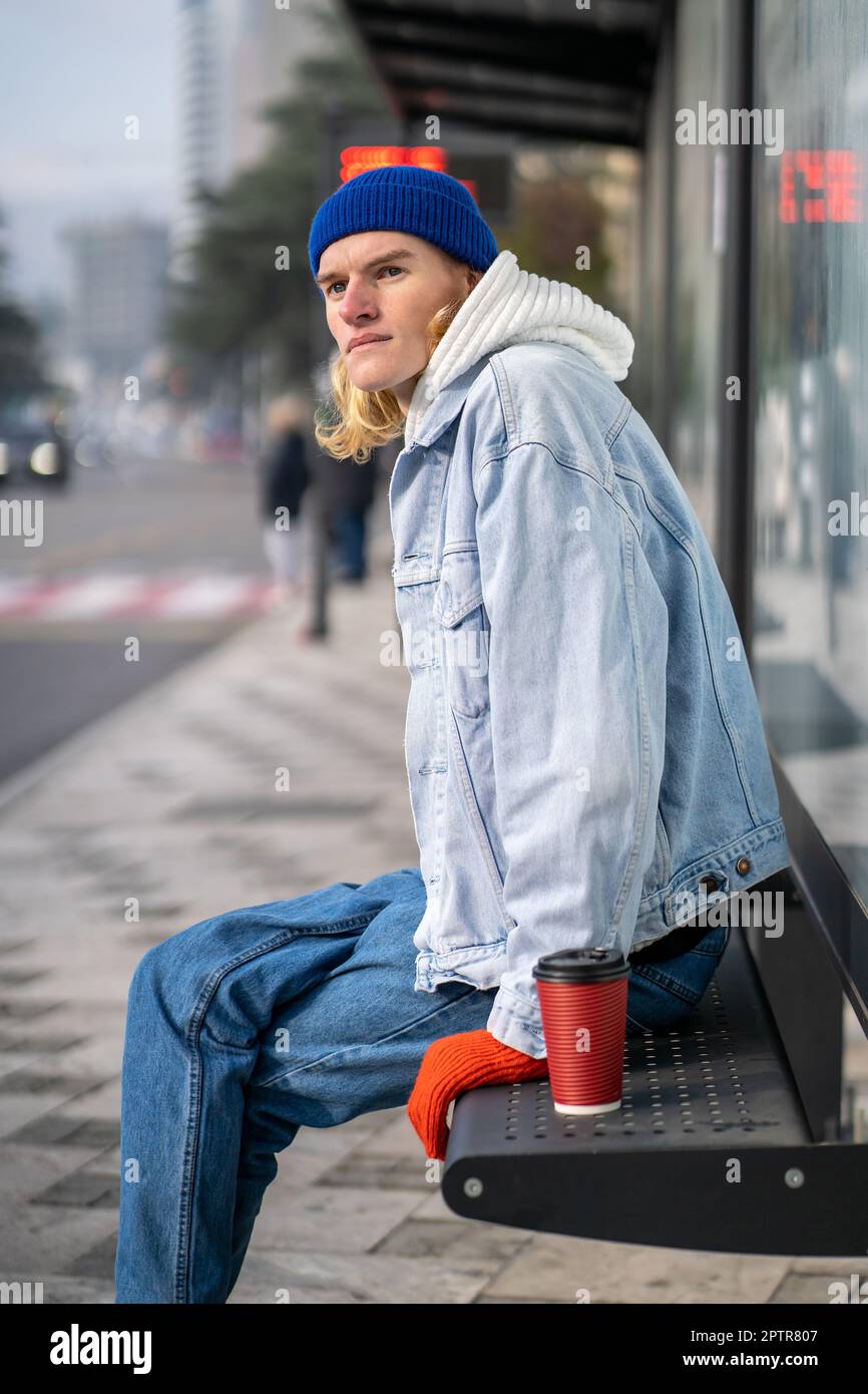 Pensive European hipster guy sitting with take away coffee on bench at ...