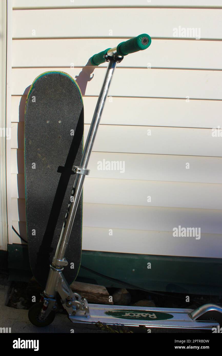 A green razor scooter and a skateboard resting against the white siding ...