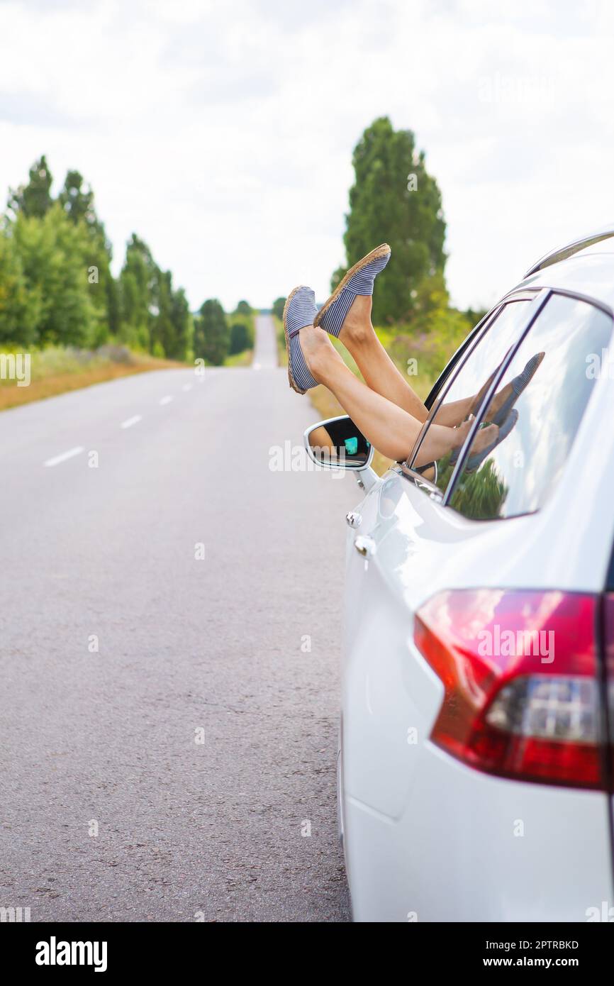 A young girl driving a car, pulling her legs out of the window, resting ...