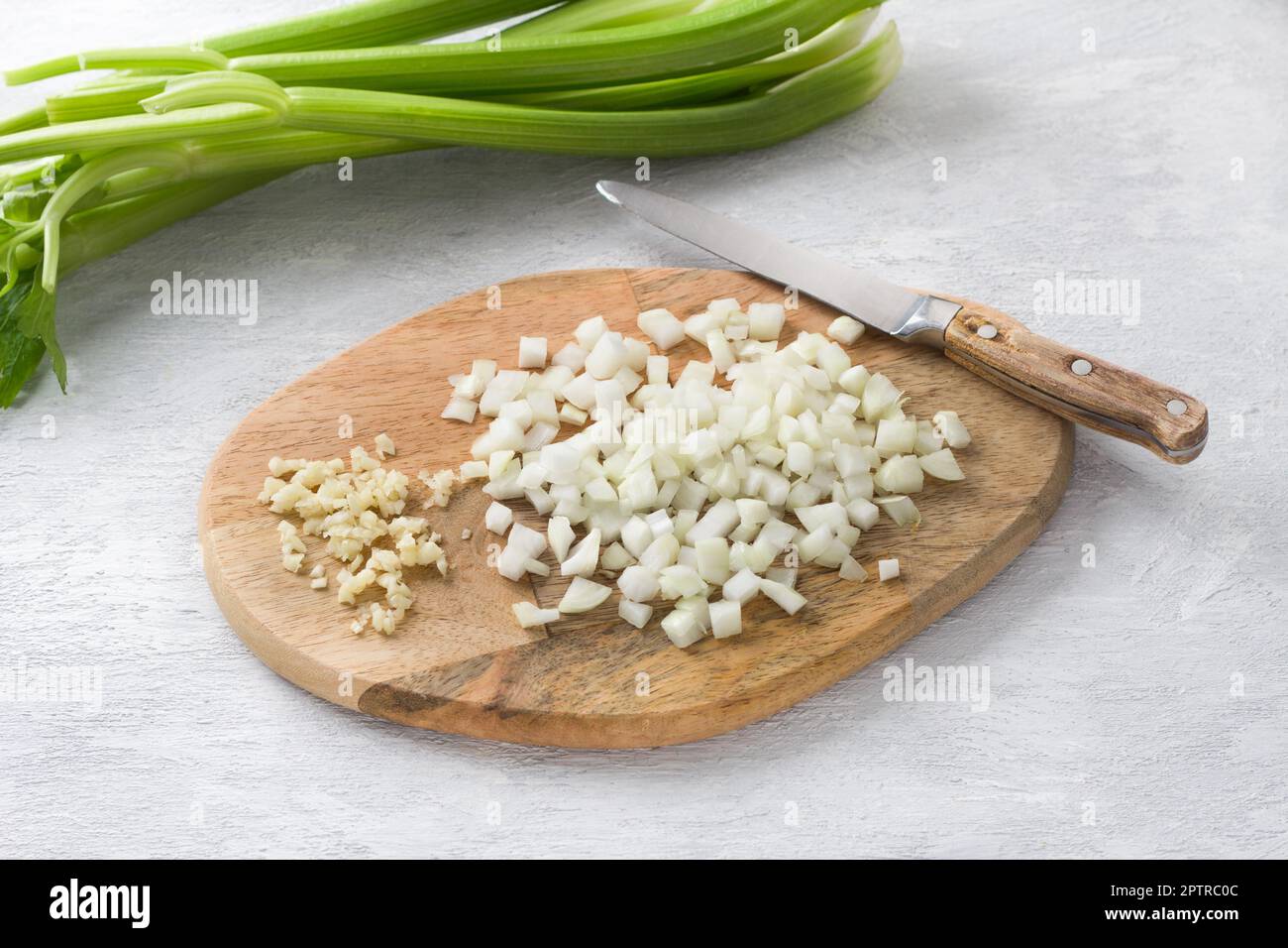 Wooden board with chopped onion and garlic, stalk celery and a kitchen ...