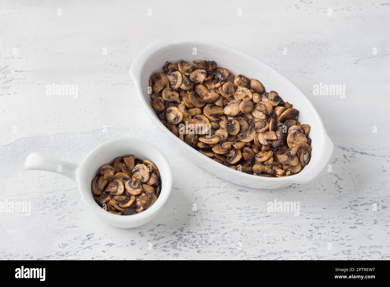 Fried champignon mushrooms in a greased form on a light gray background ...