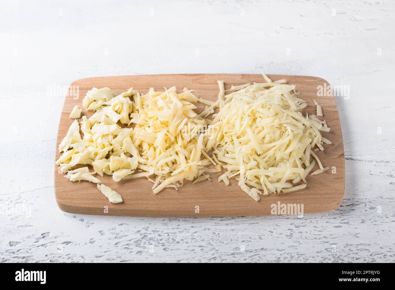 Wooden board with three types of grated cheese on a light blue ...