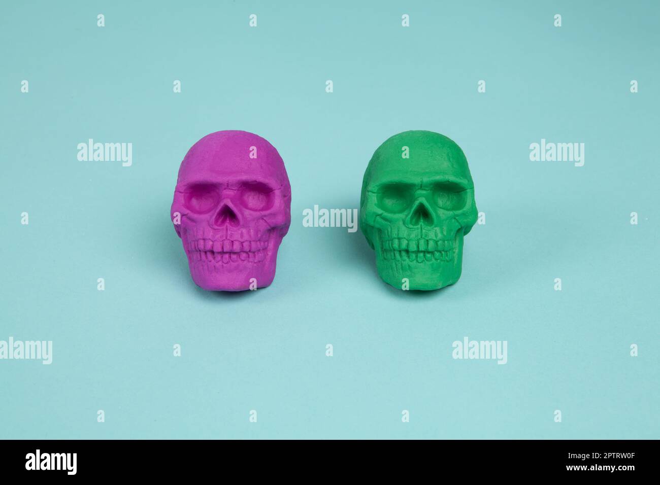 Two plastic skulls, one pink and one green, placed on a turquoise ...