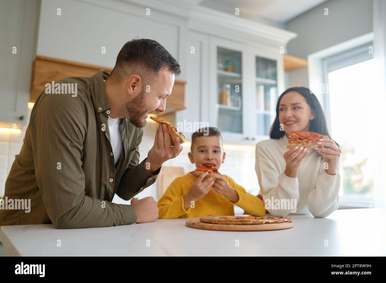 Parents and child eating delicious pizza in living-room at cozy home ...