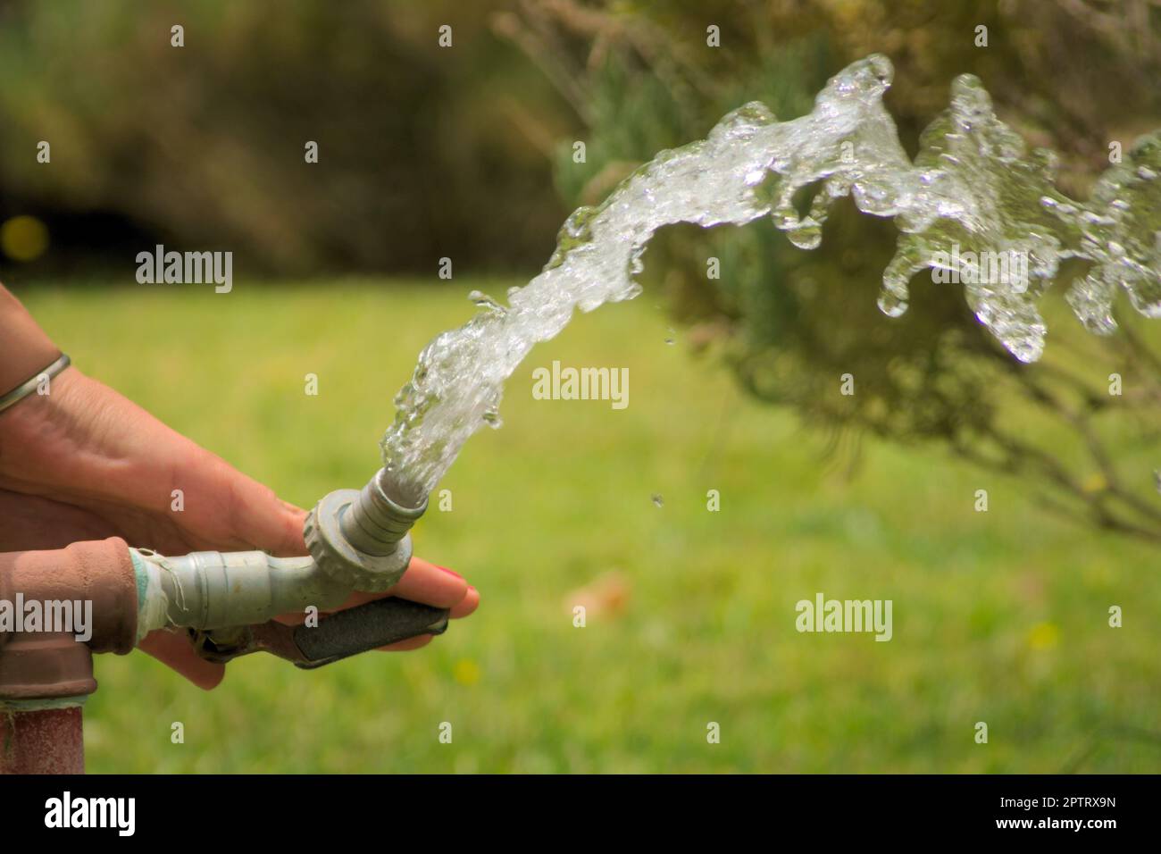 Water flowing from an outside metal faucet. A hand is closing the ...