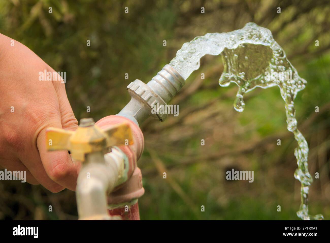 Water flowing from an outside metal faucet. A hand is closing the ...