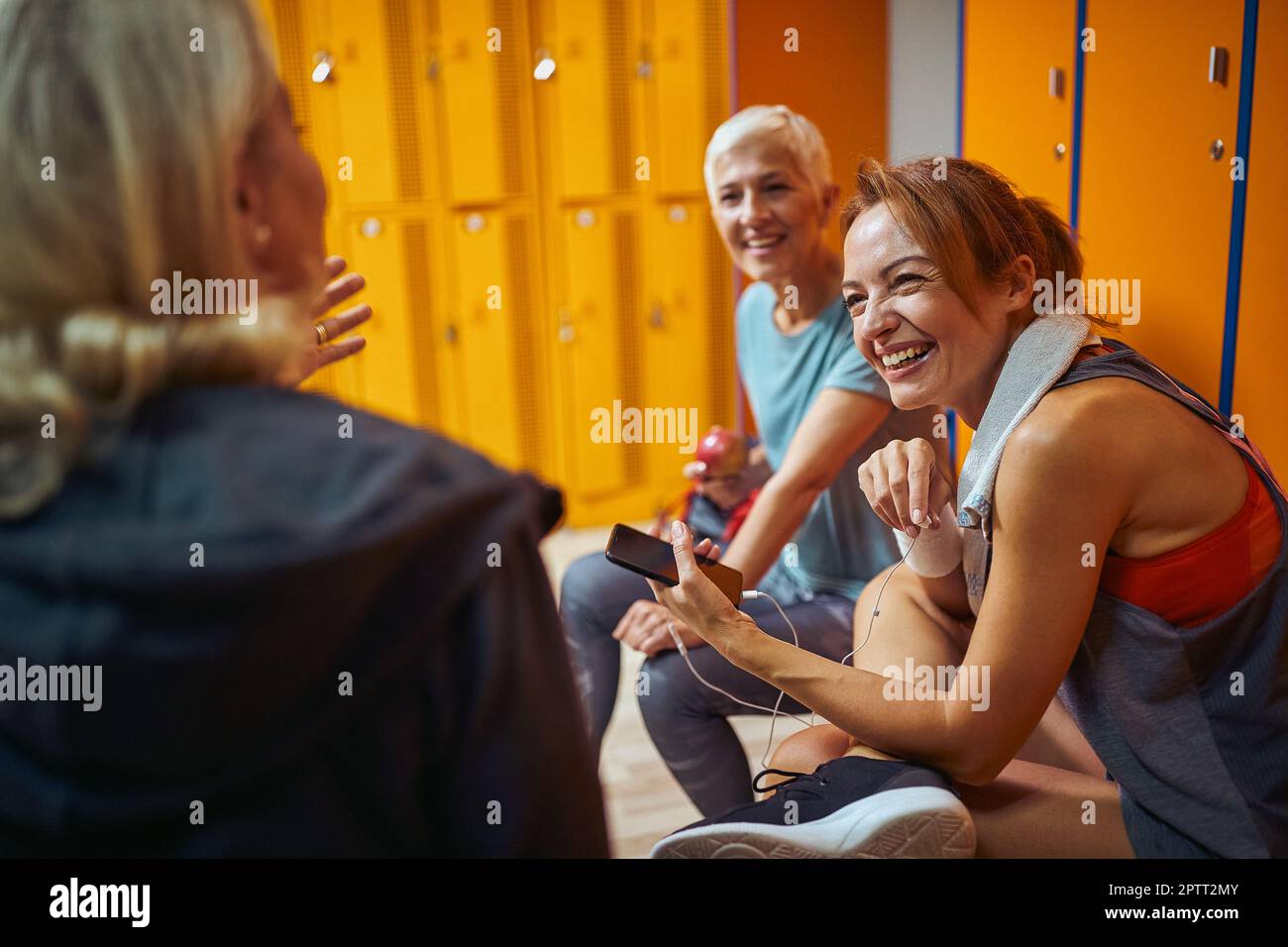 Young joyful woman trainer talking with two senior woman in dressing ...