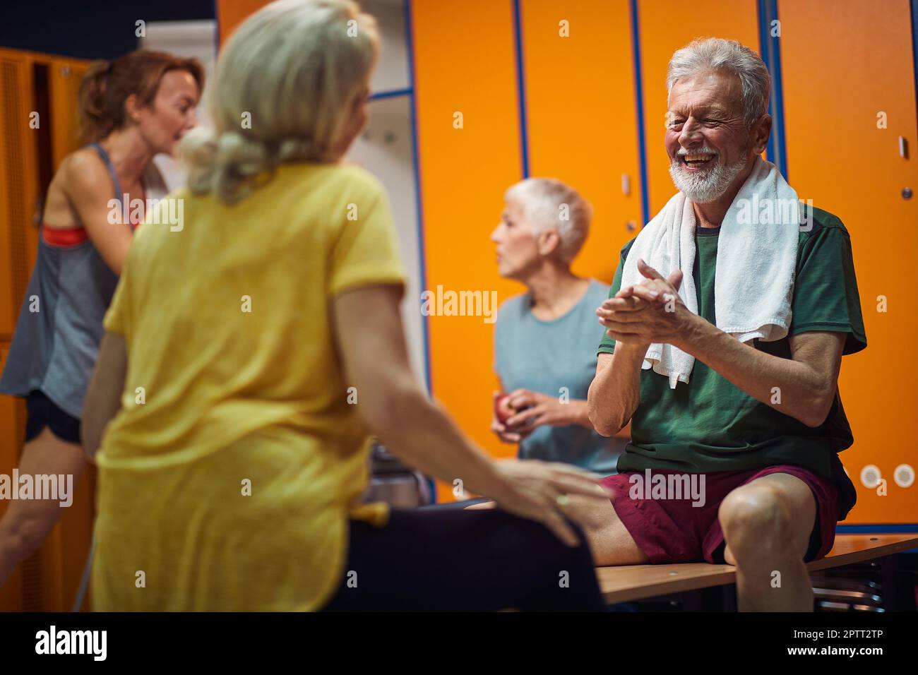 Group of four people in gym locker room, senior man and woman having a ...