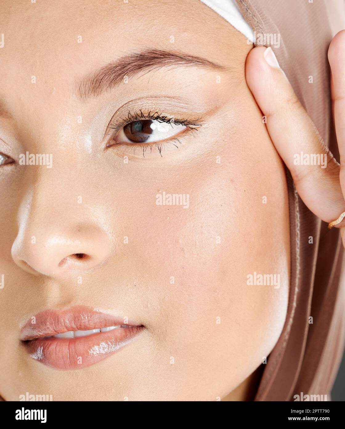 Face of a beautiful Muslim woman wearing a brown headscarf and lifting the skin around her eyes ...