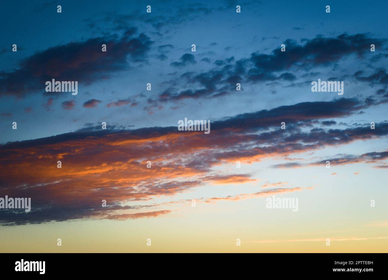 Twilight sky with dark sparse clouds receiving the last rays of ...