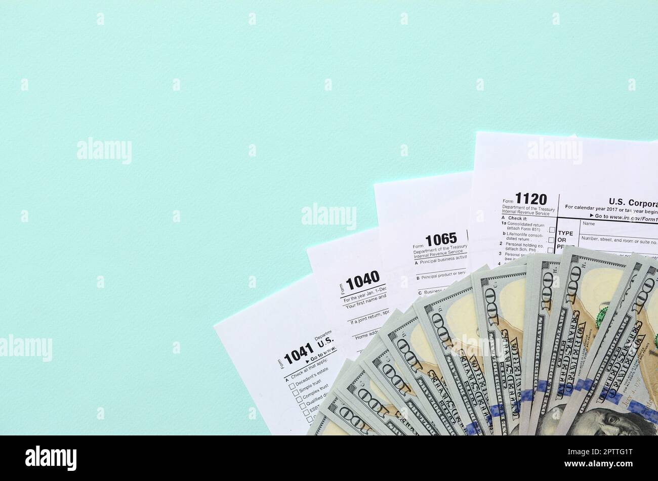 Tax forms lies near hundred dollar bills and blue pen on a light blue ...