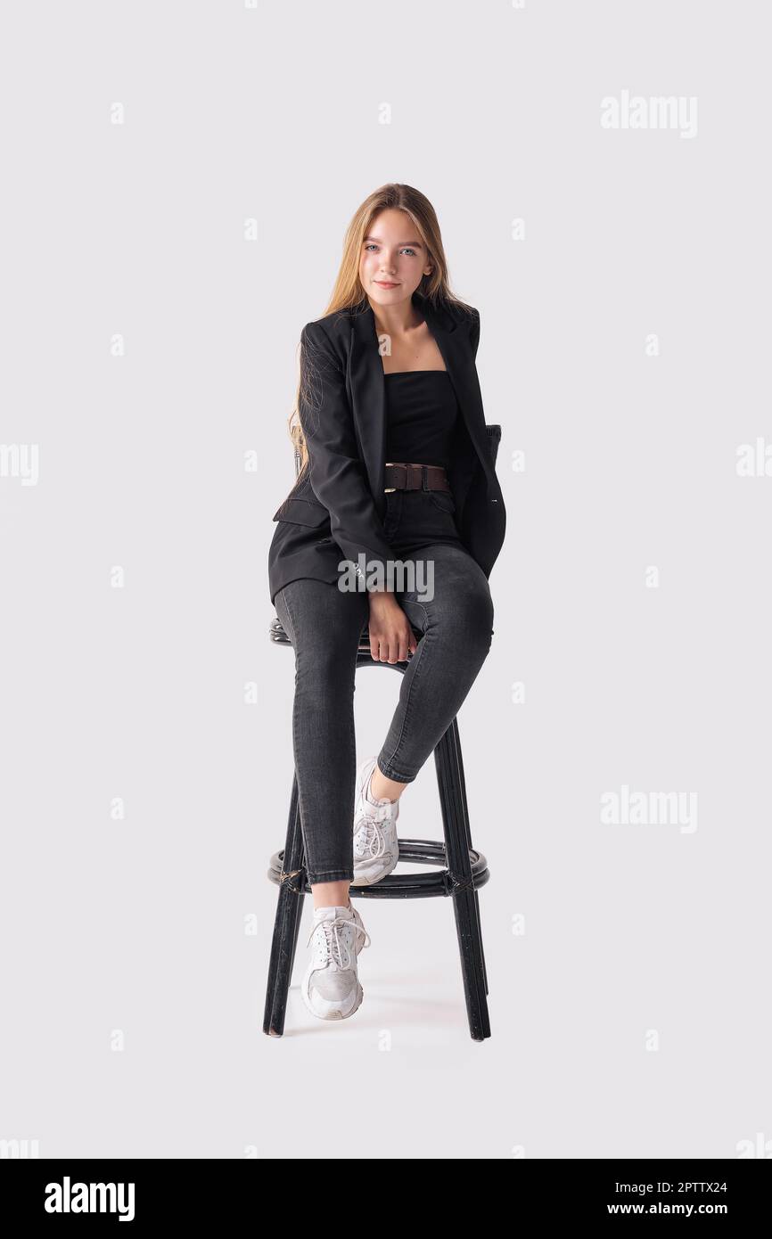 Full length portrait of beautiful young girl sitting on tall chair in ...