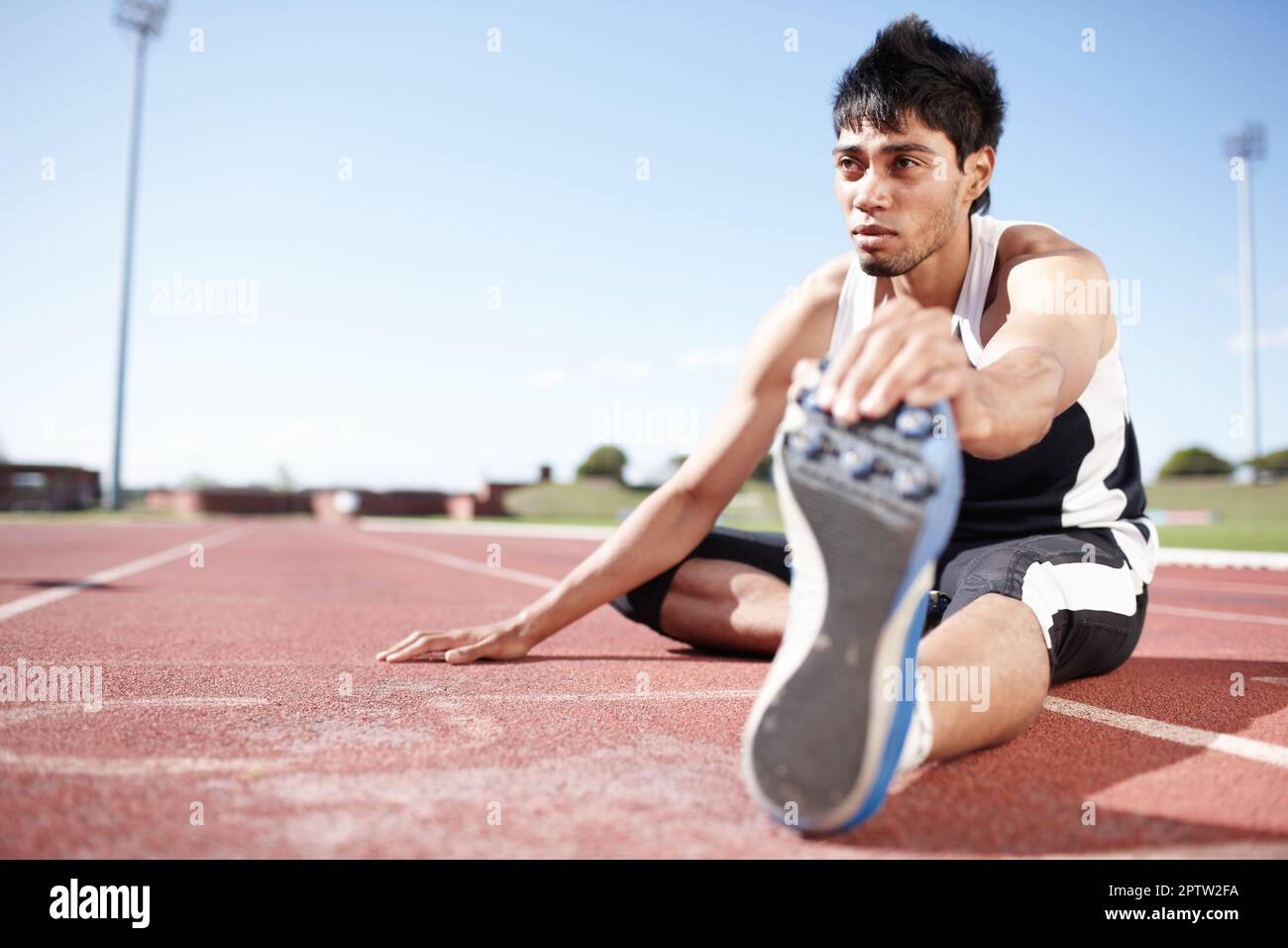 Stretching before a race. A young runner stretching his leg muscles ...