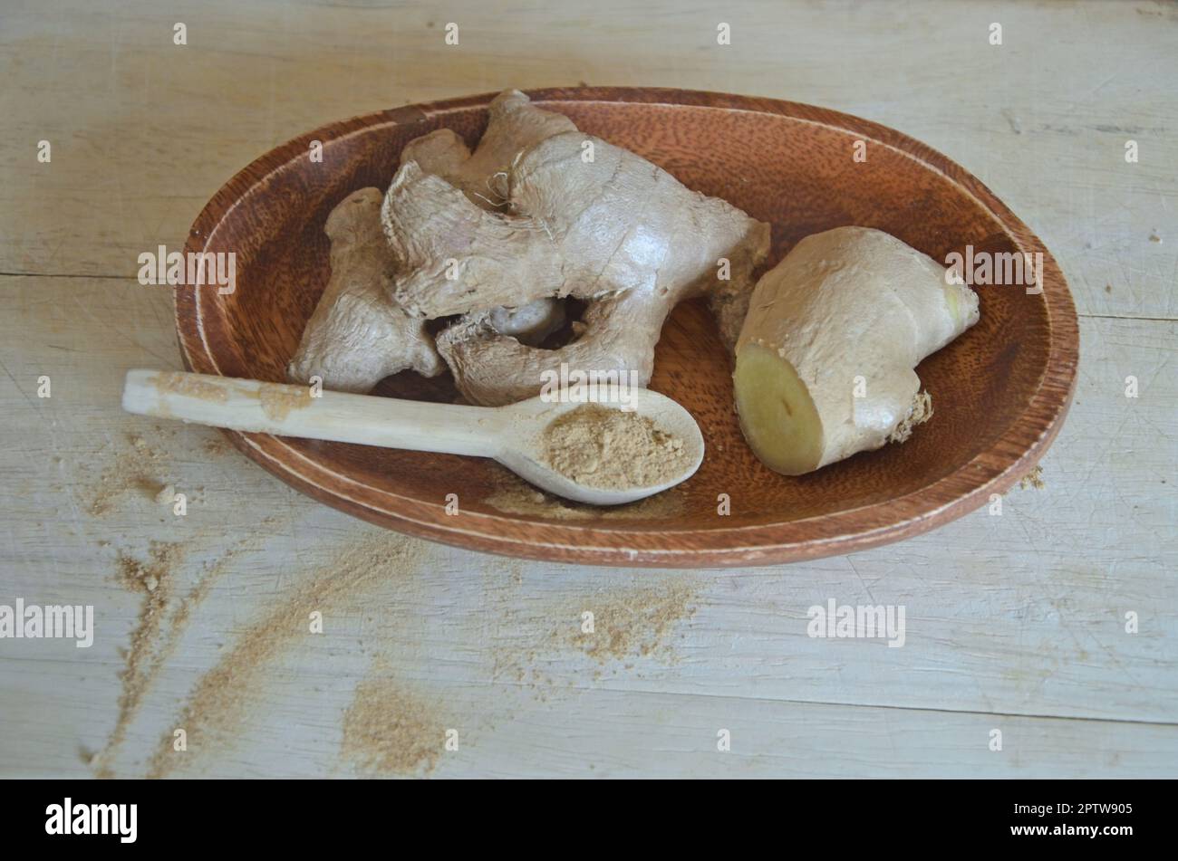 Fresh ginger root and slices, and crushed dried ginger in wooden bowl ...