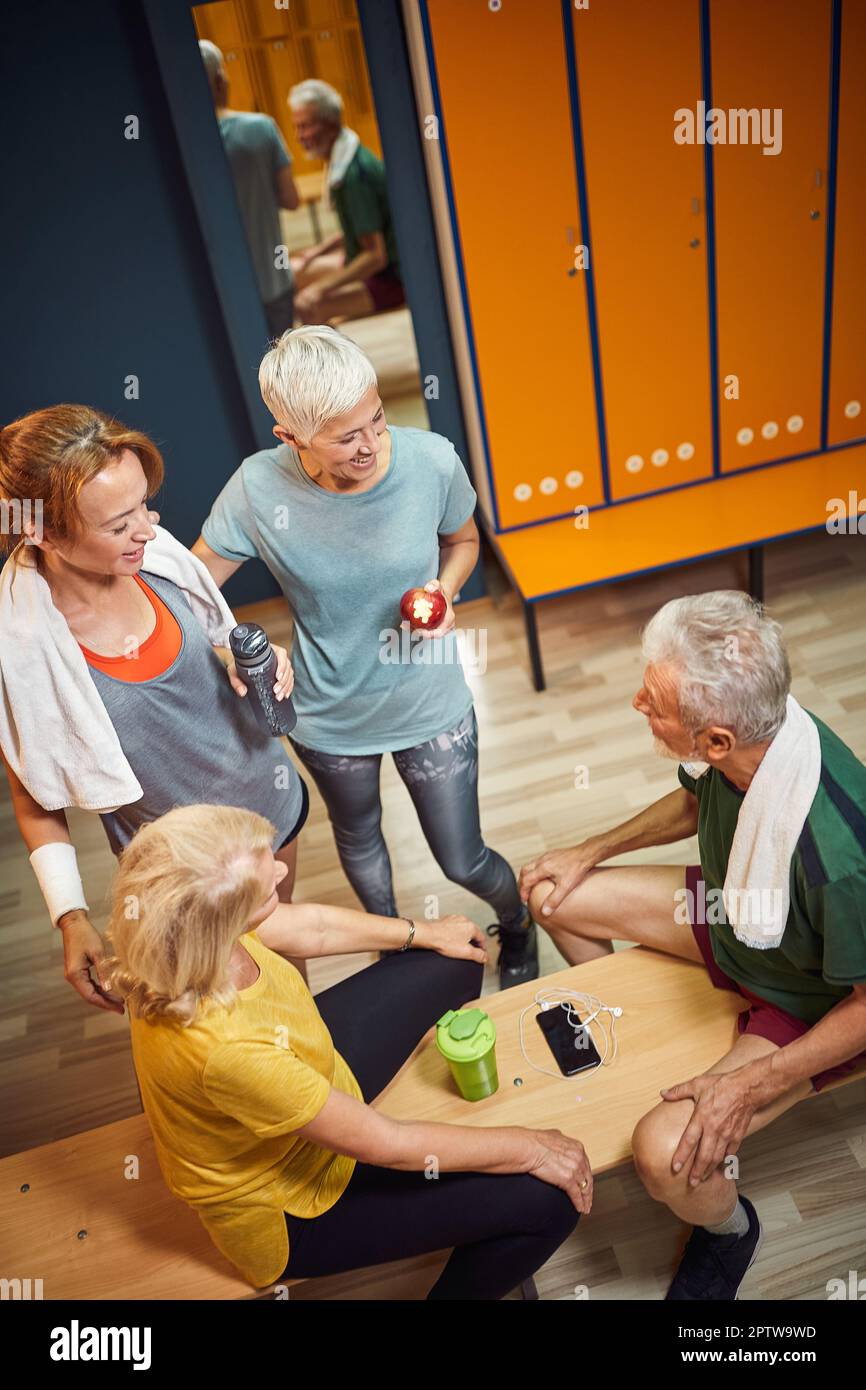 Vertical top shot of four people in gym locker room together enjoying ...