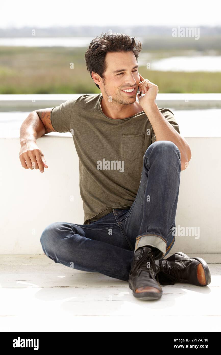 Making a call outside. A handsome young man sitting outside and making ...