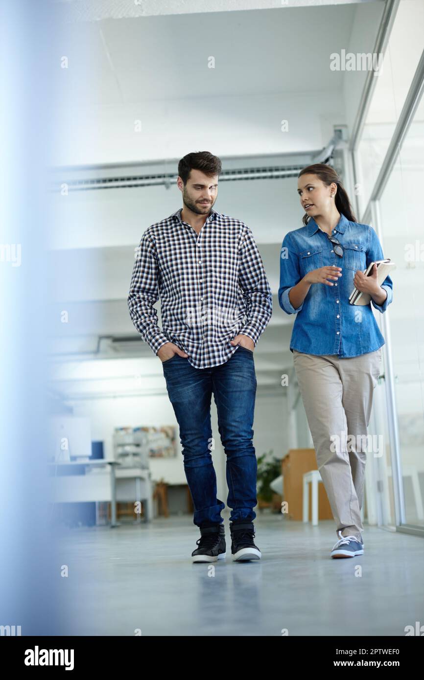 Heading out. two colleagues talking while walking in the office Stock ...
