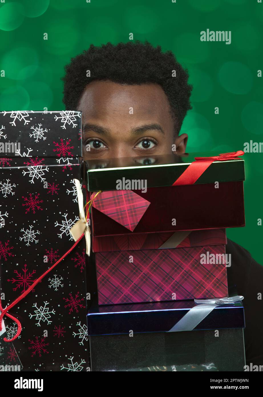 young man hidden behind gift boxes for christmas night holding present ...