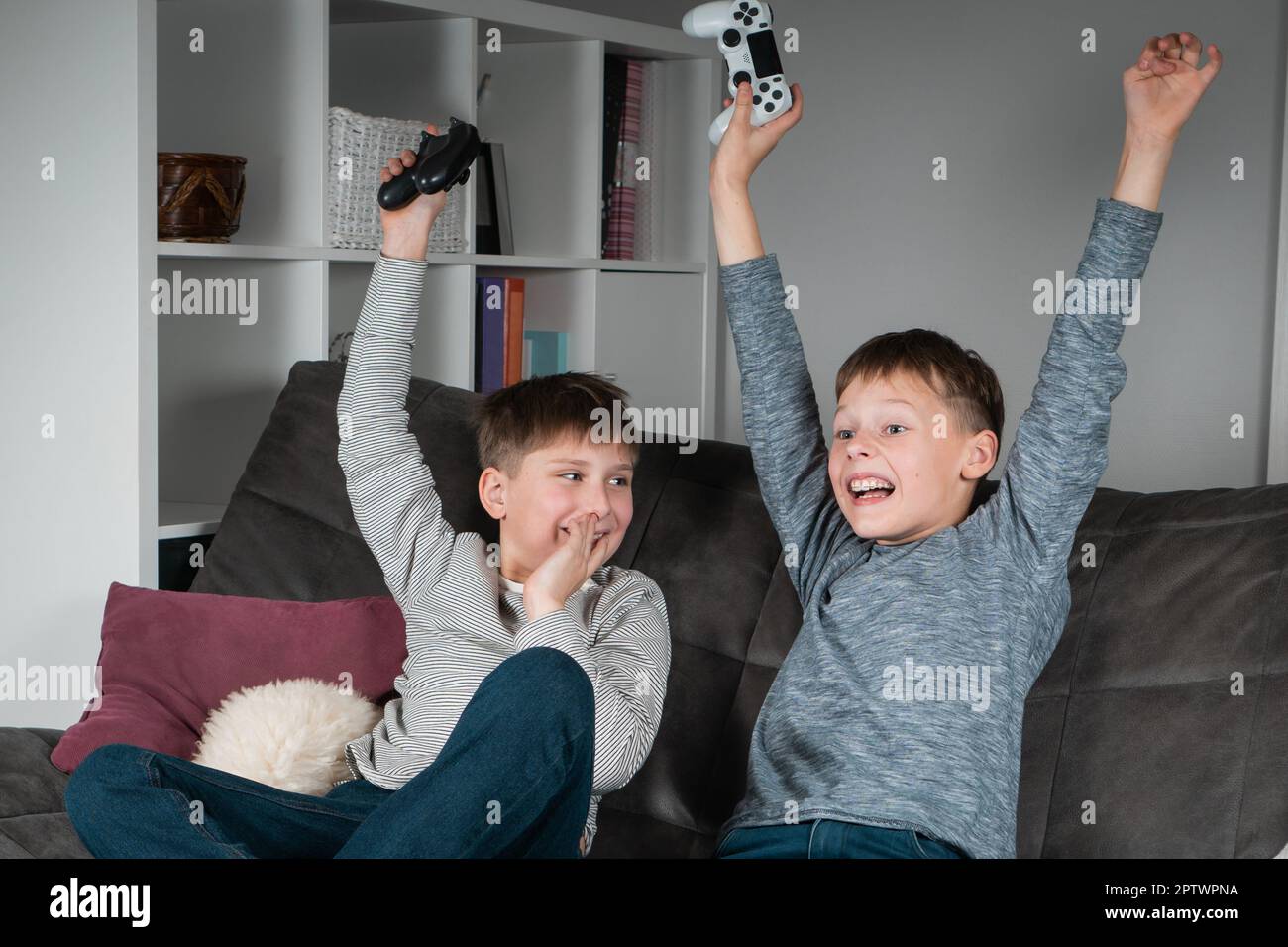 Portrait of two wonderful positive teenage boys sitting on grey sofa at ...