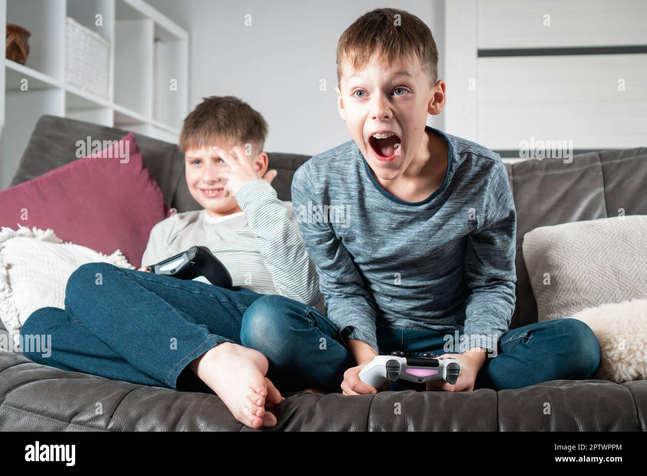 Portrait of two excited teenage boys children sitting on grey sofa at ...
