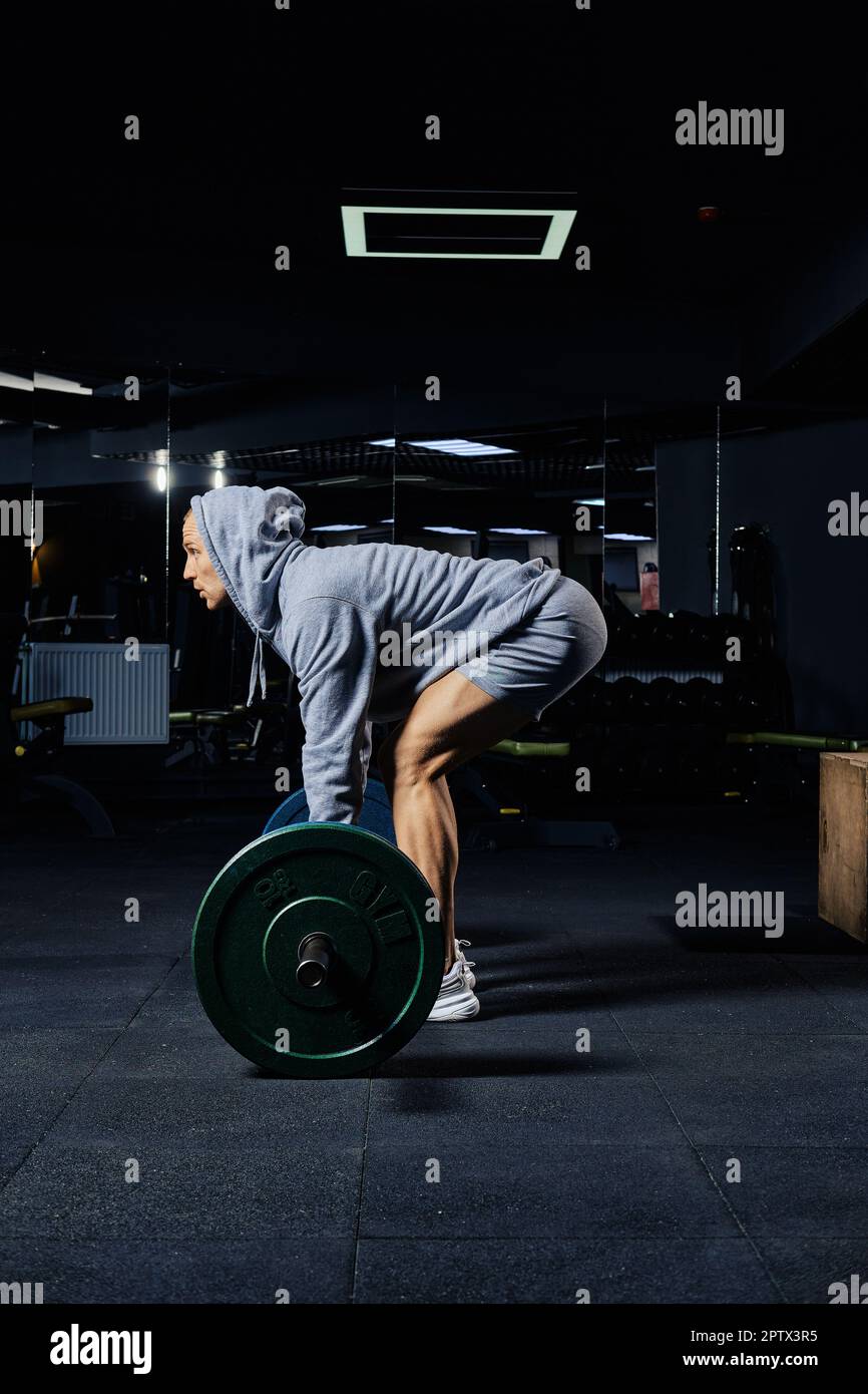 Muscular man doing deadlift exercise with barbell in gym, side view ...