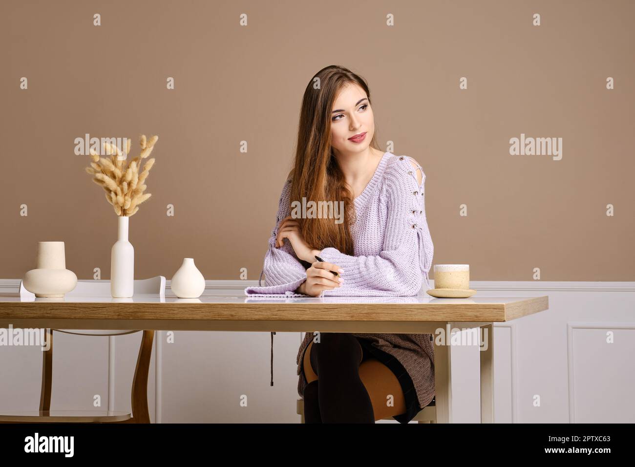 Pensive young woman sits behind the table and thinking about what to ...