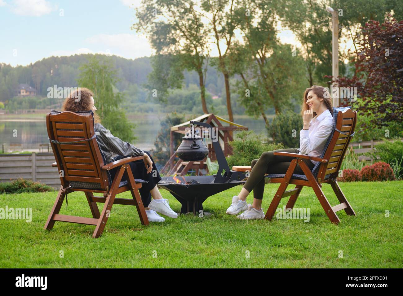 Two women are relaxing in the backyard, sitting in chairs and chatting ...