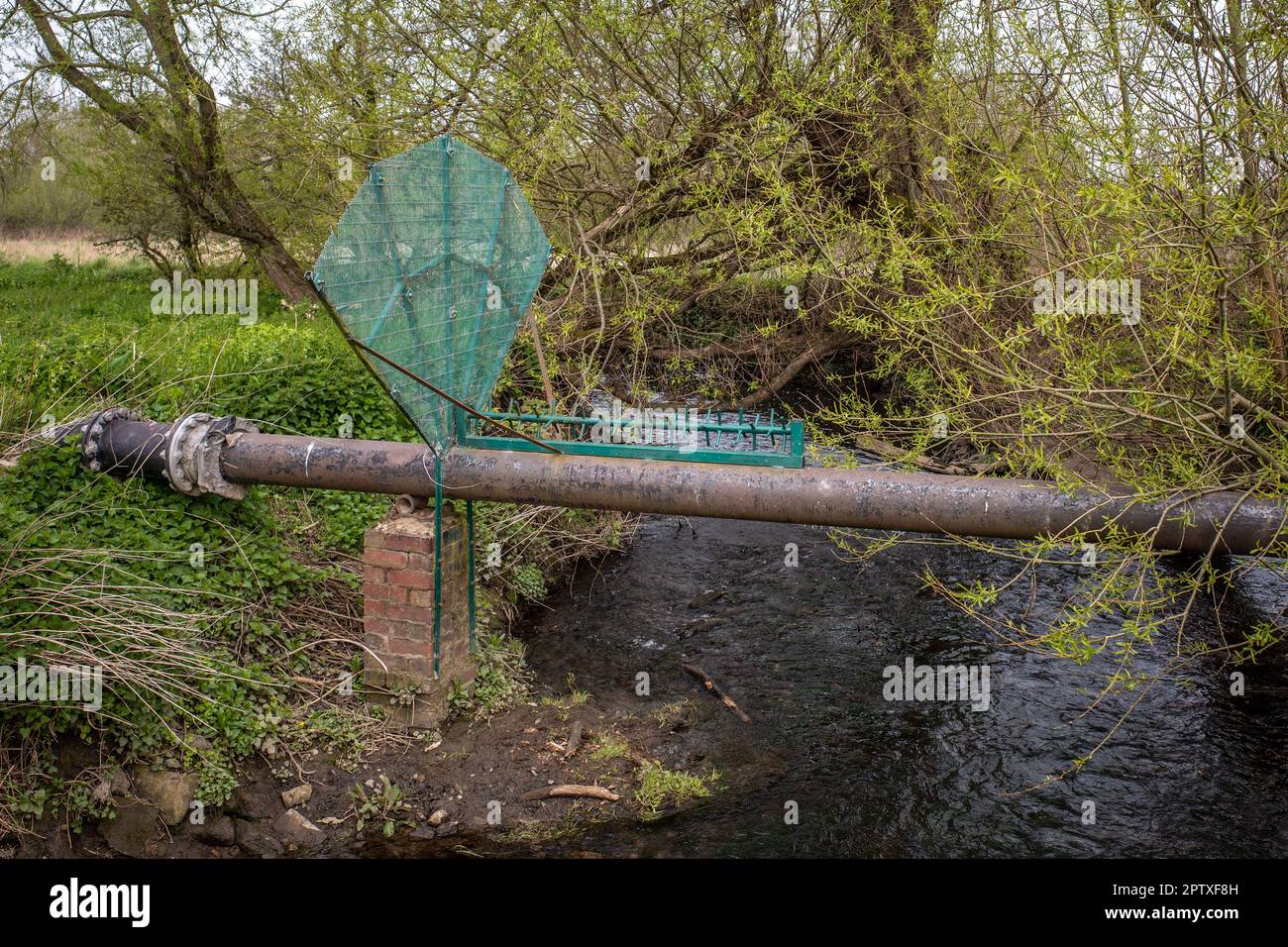 A large pipe crossing a stream with a green safety guard and spiked ...