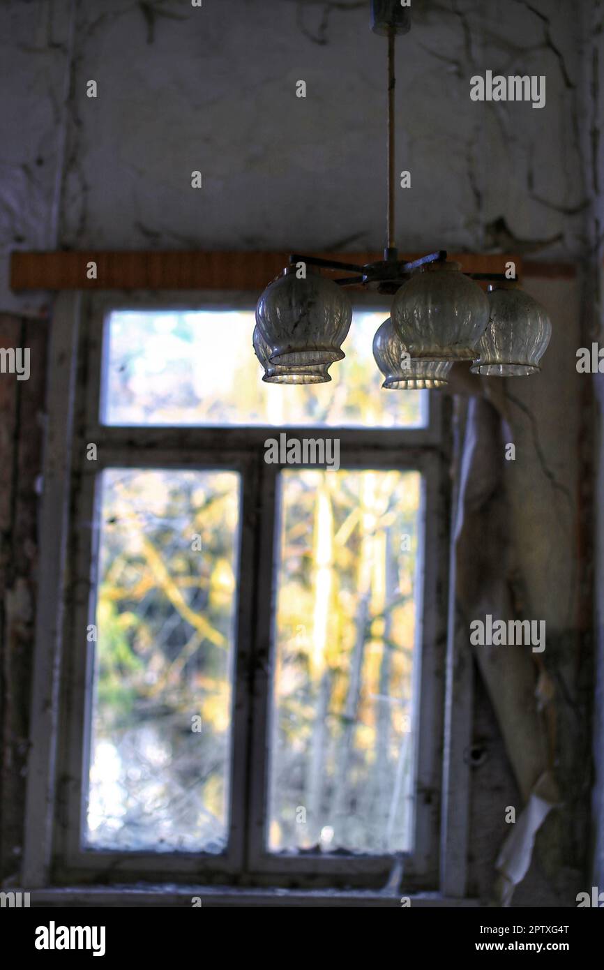 Ceiling lamp hanging in a dirty and desolate room with window, slanted ...