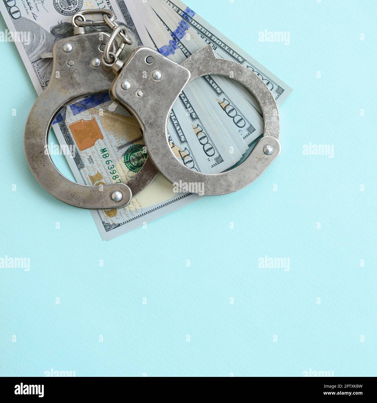 Silver police handcuffs and hundred dollar bills lies on light blue ...