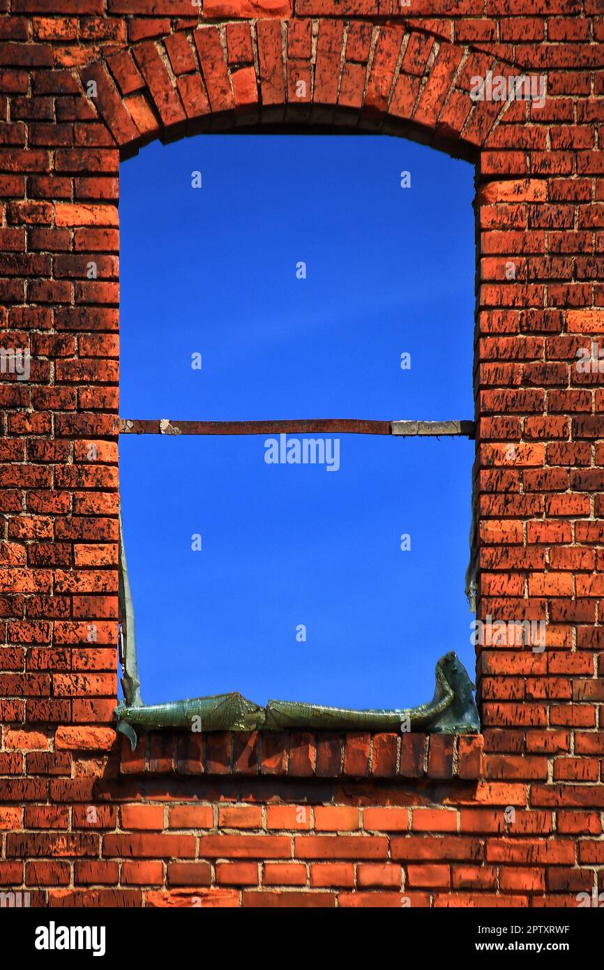Window frame in brickwall with blue sky, the glass is molten due to a ...