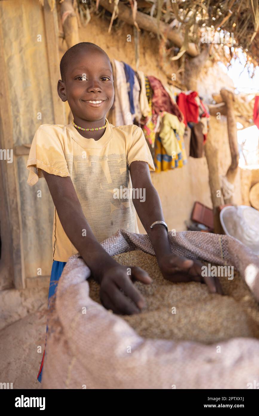 A boy scoops his hands into a bag of millet grain at his home in Segou ...