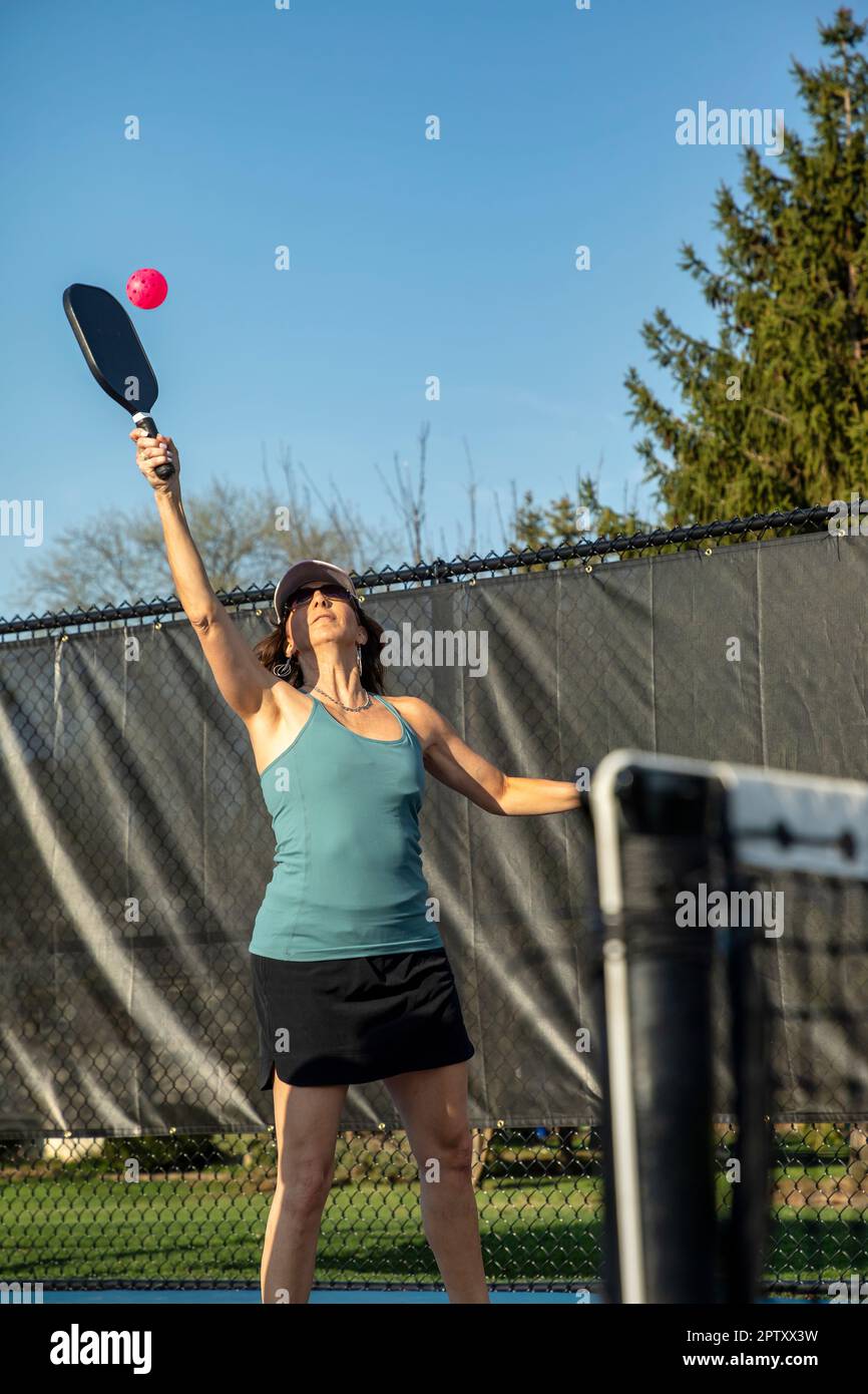 A female pickleball player returns a high volley of a bright pink ball ...
