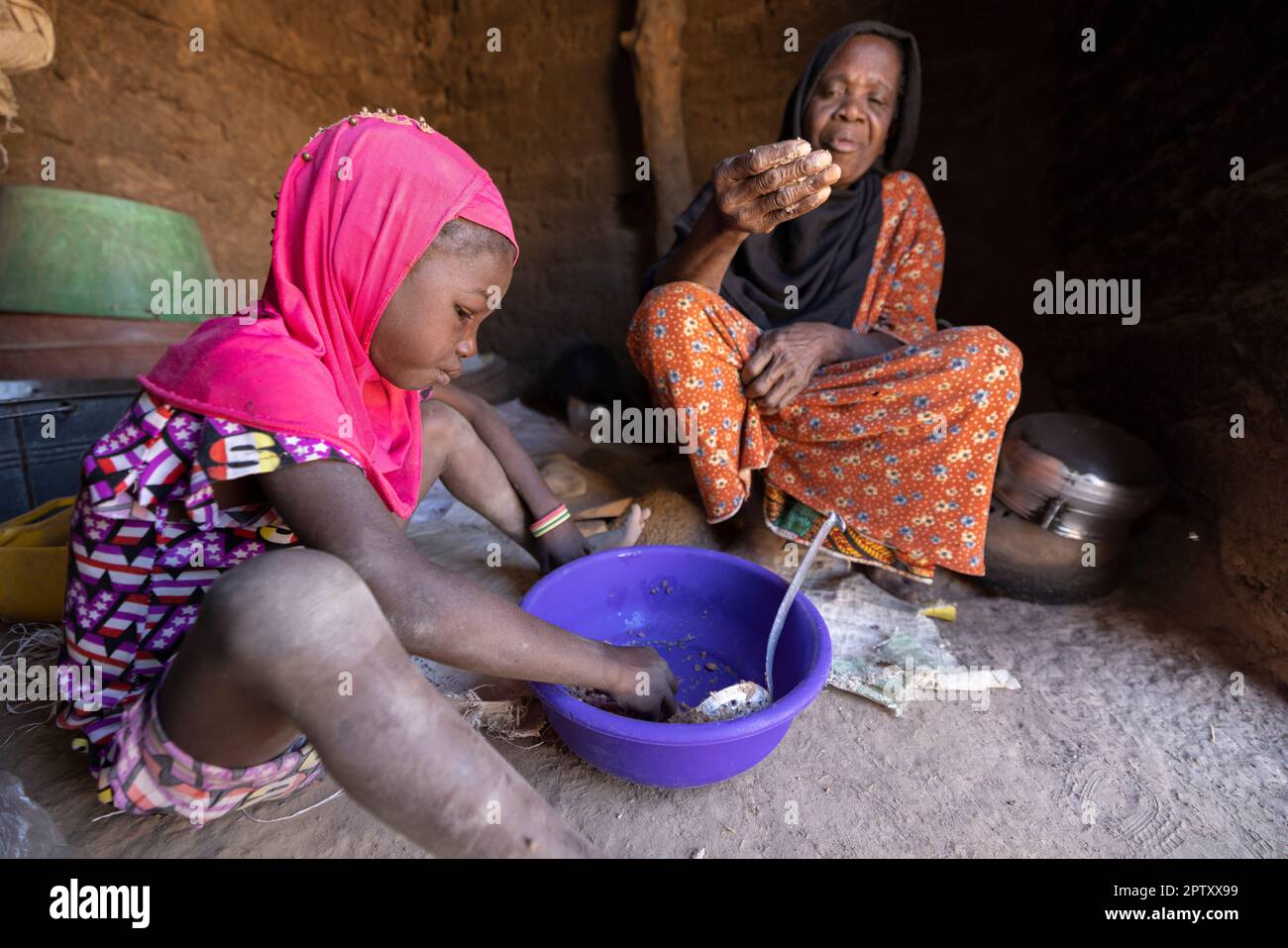 A young child and her grandmother eat a meager meal on the floor of ...