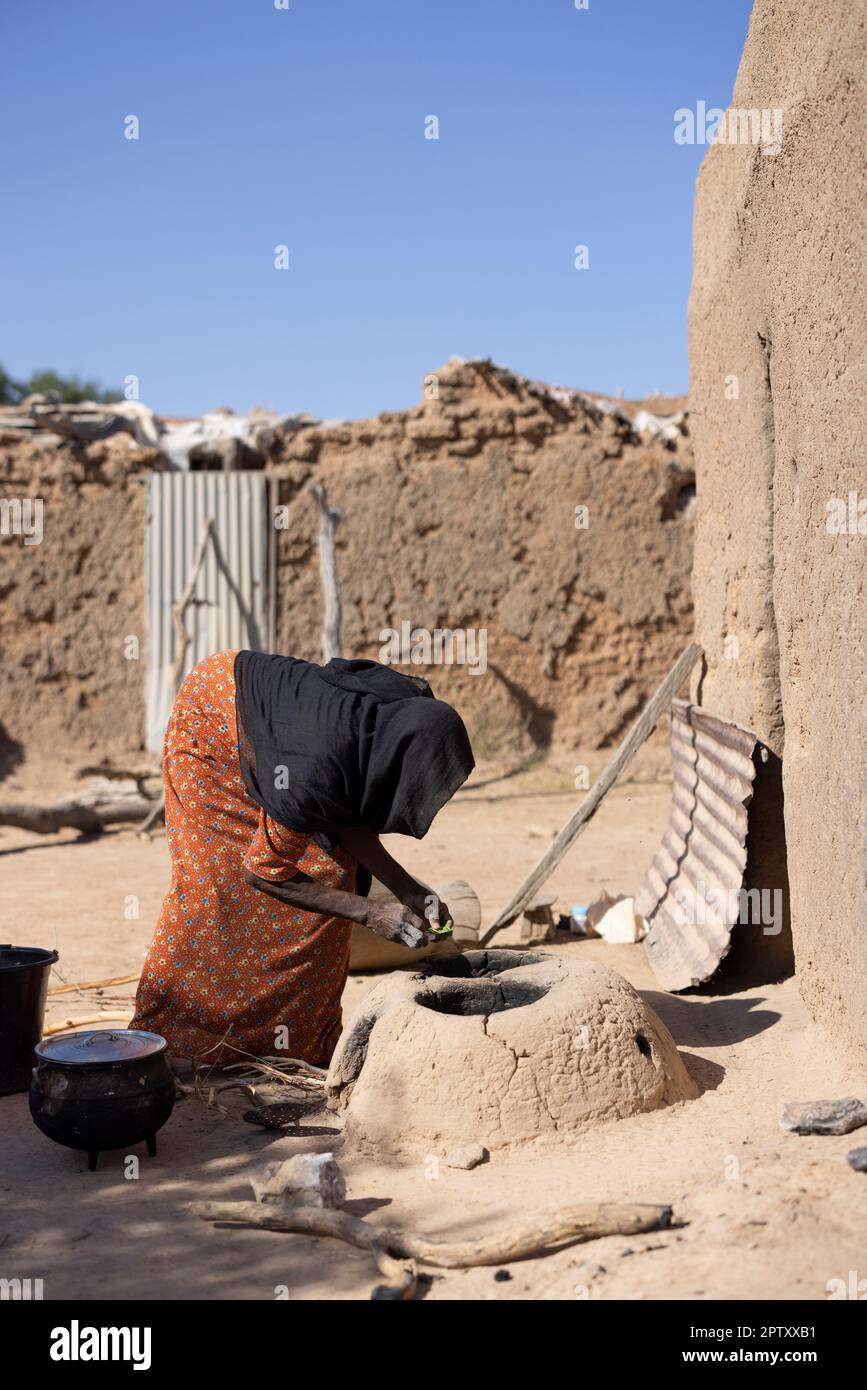 A woman lights a fire in her adobe mud cooking stove outside her house ...