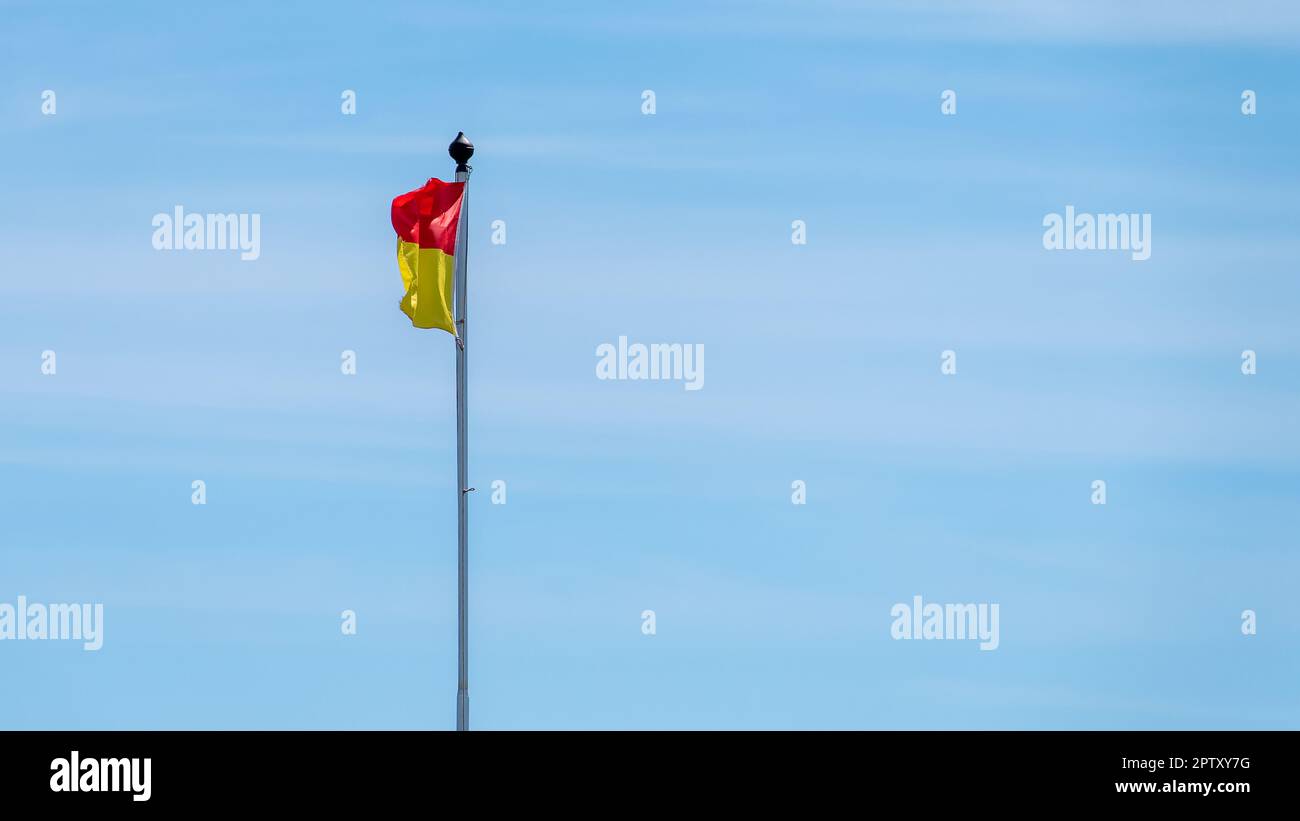 A red and yellow flag allowing swimming on the beach. flag on a sky ...