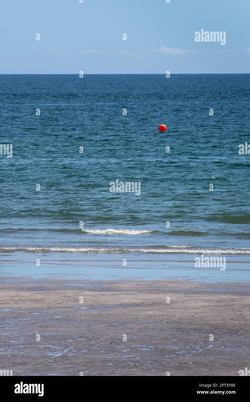 Blue sea water and a sandy beach under a blue sky. Orange buoy on the ...
