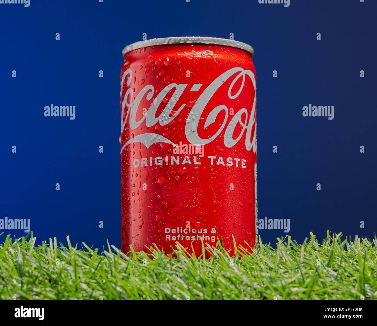 Can of cold coca-cola resting on some grass with a blue background ...