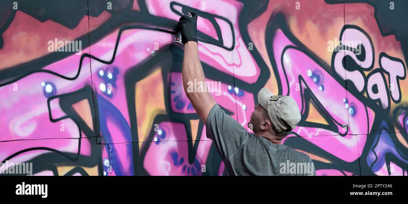 Young caucasian male graffiti artist drawing big street art painting in ...