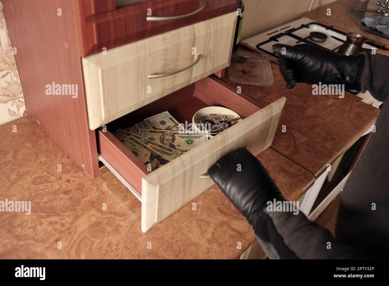 Robber in black outfit and gloves see in opened shelf in kitchen. The ...