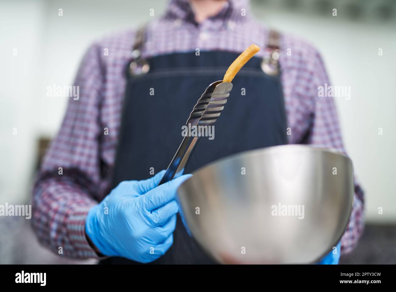 Kitchen worker holding fries with tongs. The cook preparing potato ...