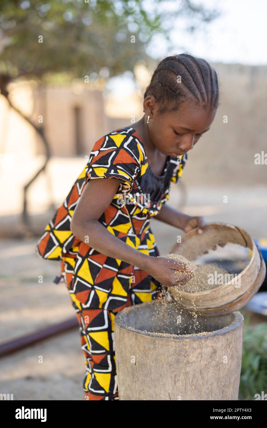 A girl child sifts millet grain while stamping it into flour in Segou ...