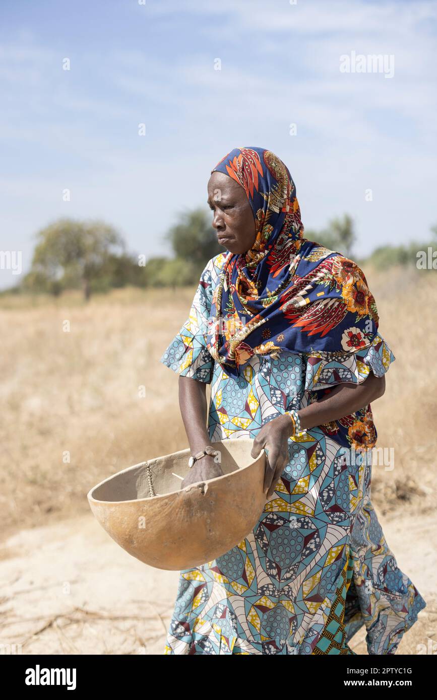 A muslim woman in traditional colorful dress winnows her millet grain ...