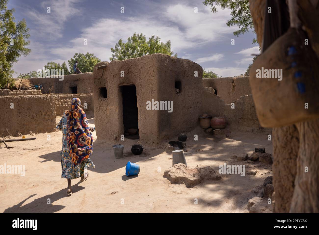 A woman walks into her adobe mud constructed kitchen in her home ...